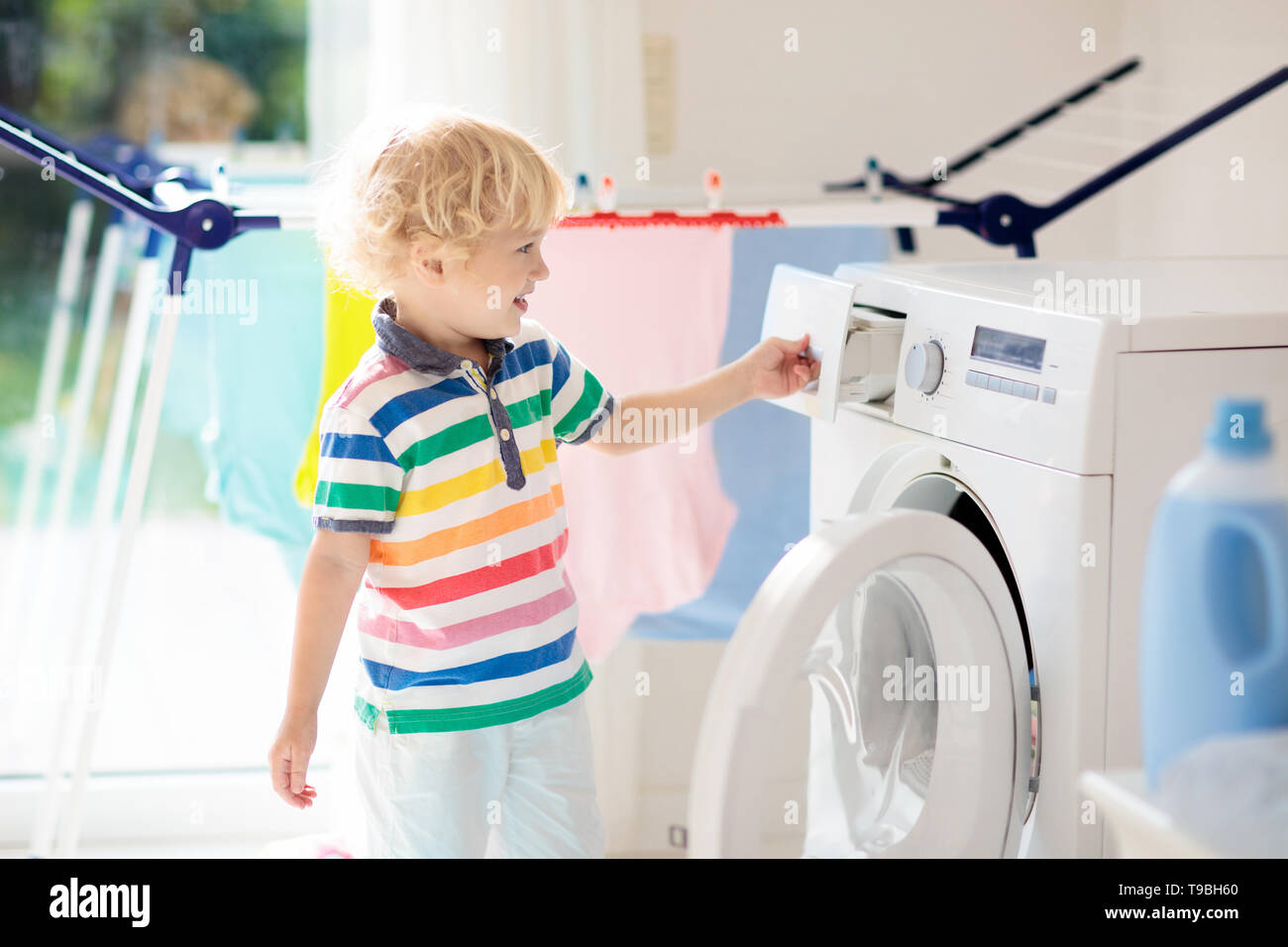 Child in laundry room with washing machine or tumble dryer. Kid helping ...