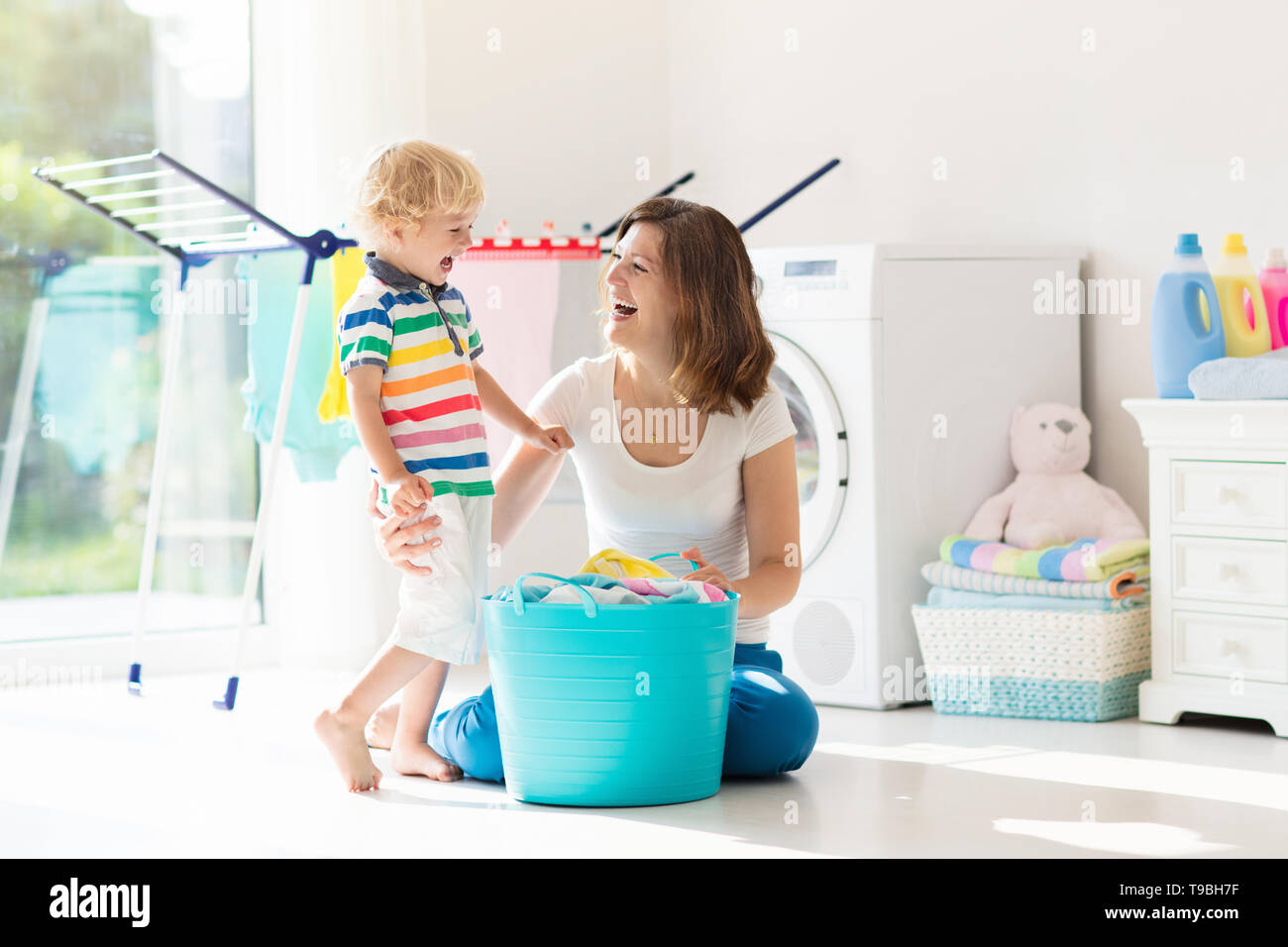 Mother and kids in laundry room with washing machine or tumble dryer ...
