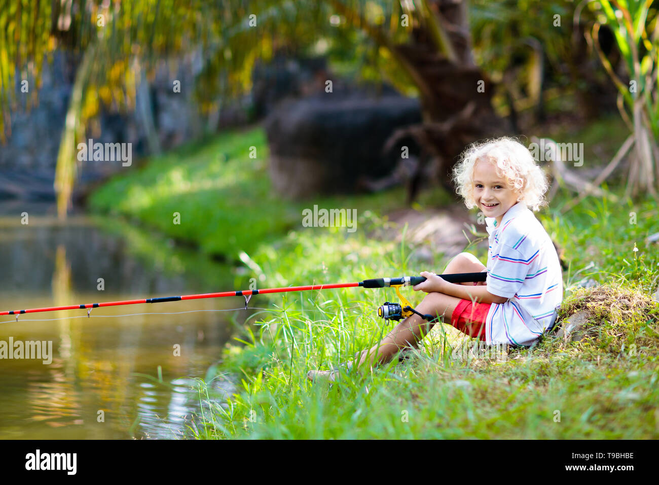 Boy fishing. Child with red rod catching fish in river on sunny summer ...
