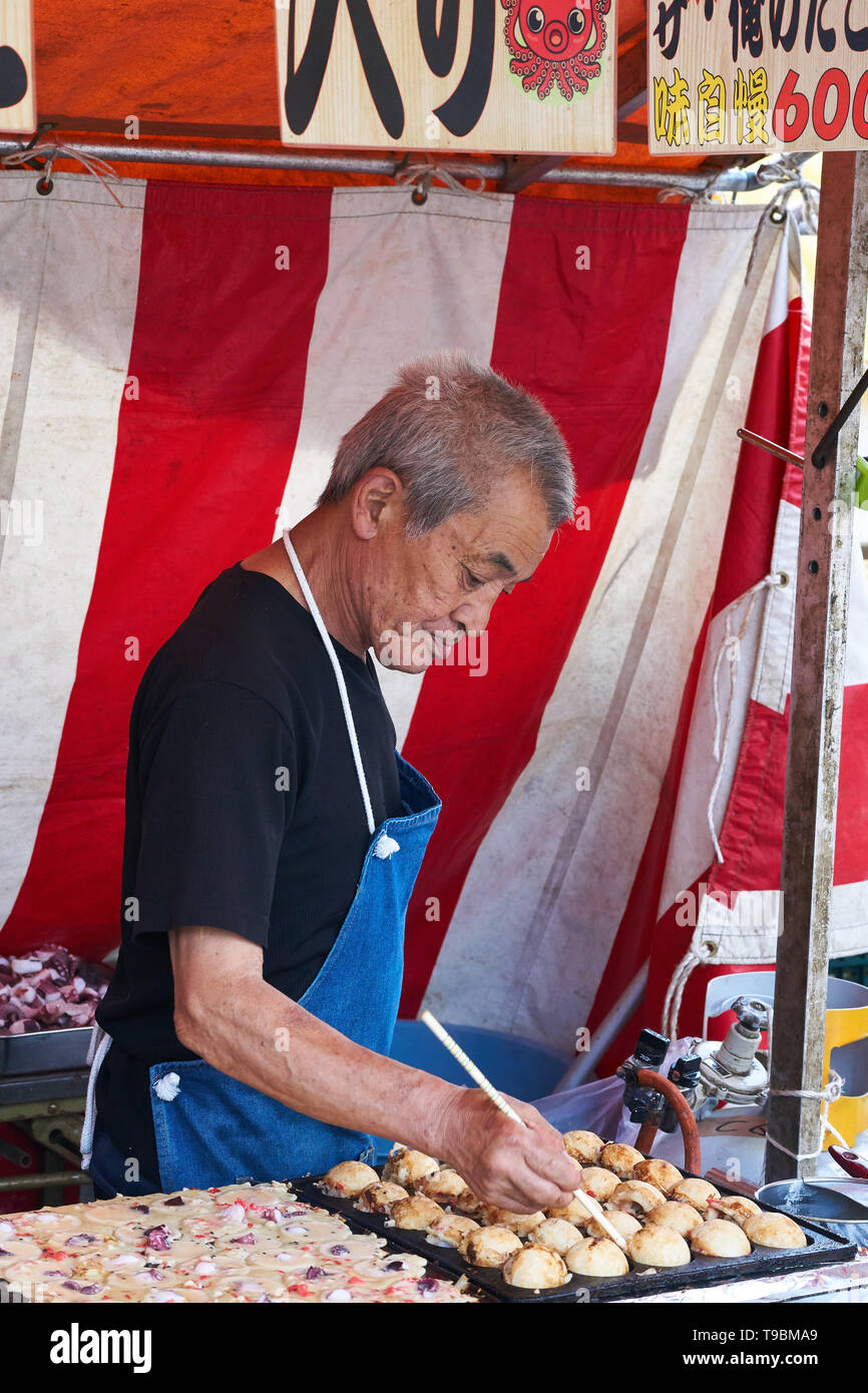 A mature Japanese man turns takoyaki (octopus balls), at a food stall ...