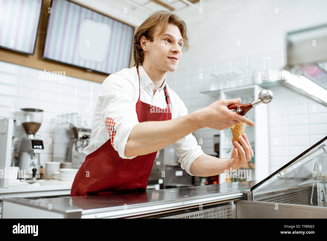 Handsome salesman in red apron selling ice cream in the modern pastry ...