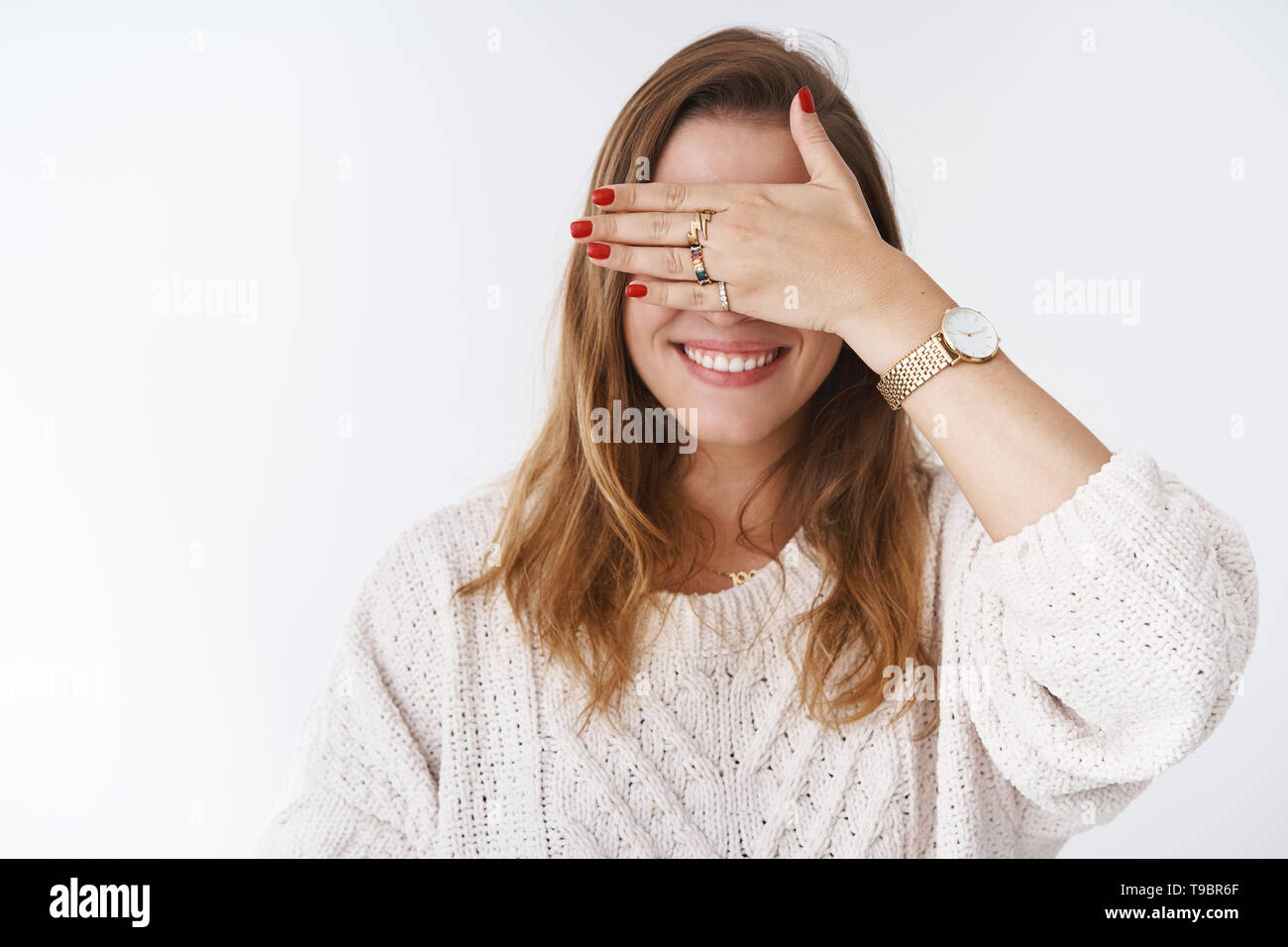 Charming caucasian girl hiding eyes behind palm smiling happily ...