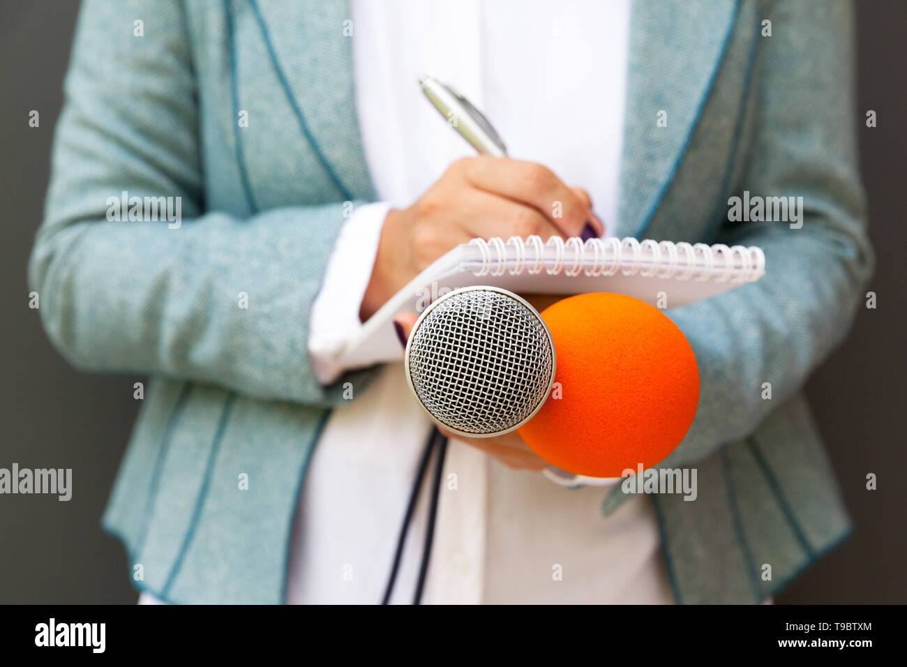 A female journalist taking notes and holding a microphone at the press ...