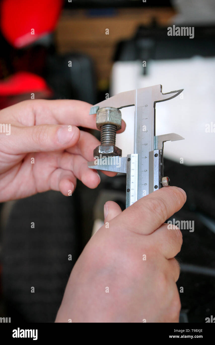 Worker with tools in hands. Mechanic is checking and measuring screw ...