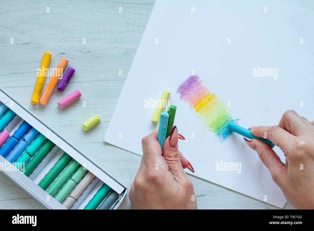 Closeup top view of female hands drawing with multicolored crayons on a ...