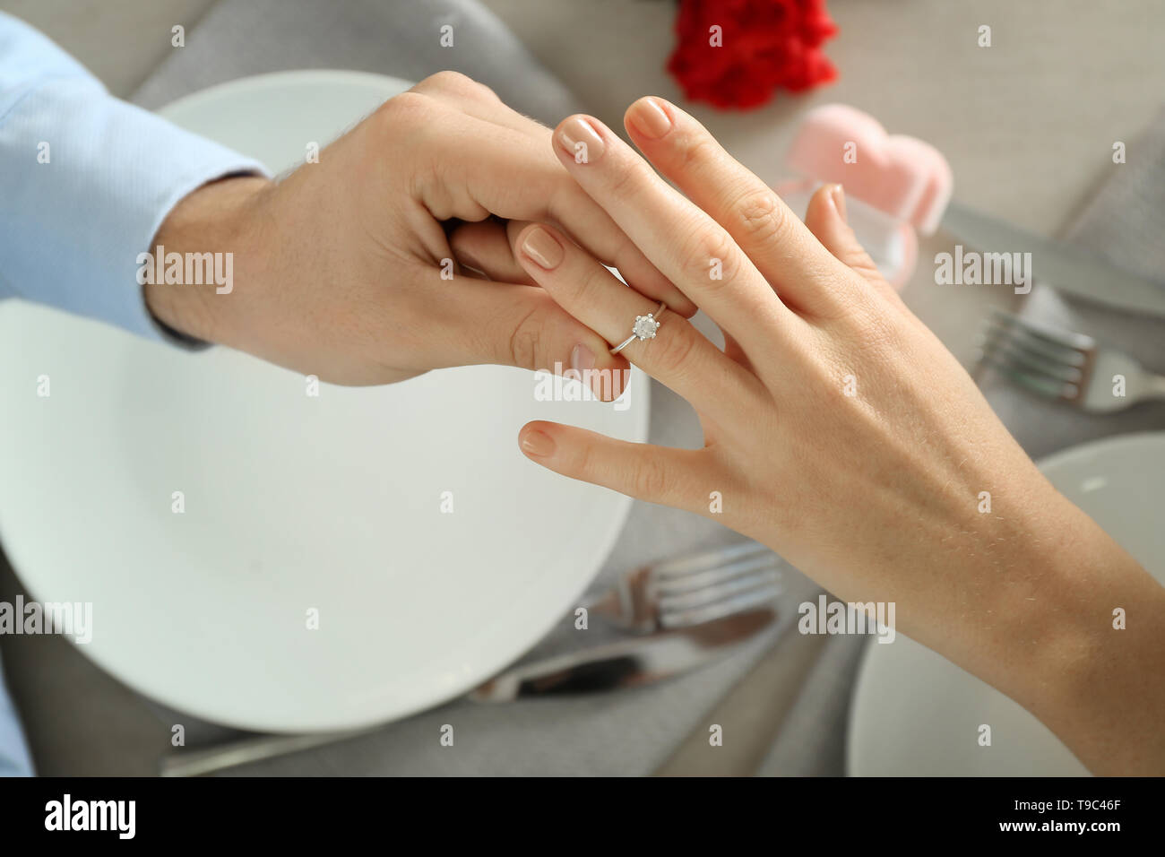 Young man putting engagement ring on fiancee's finger at romantic date ...