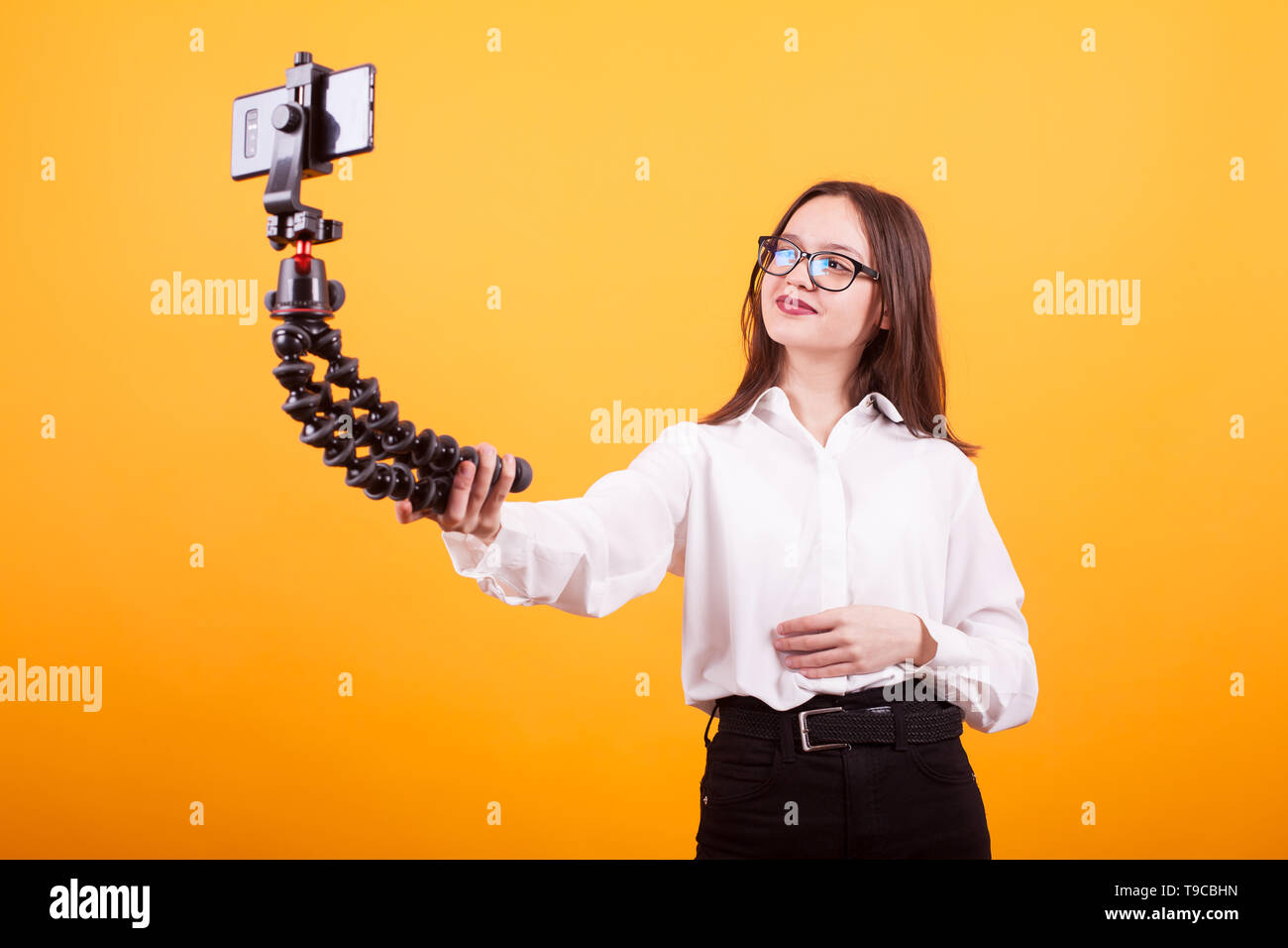 Beautiful young blogger girl taking a selfie in studio over yellow ...