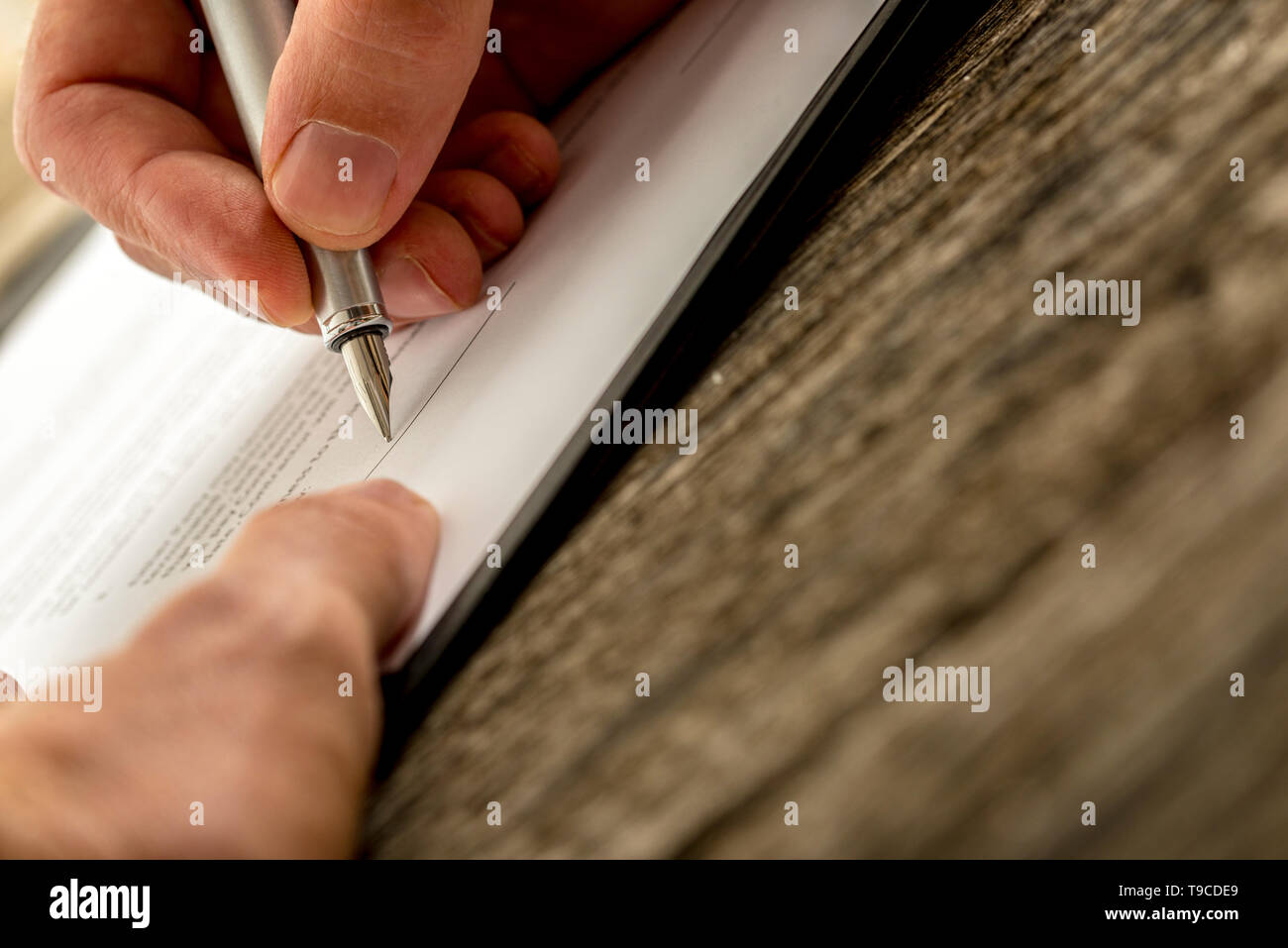 Low angle closeup view of male hand signing contract, document or ...