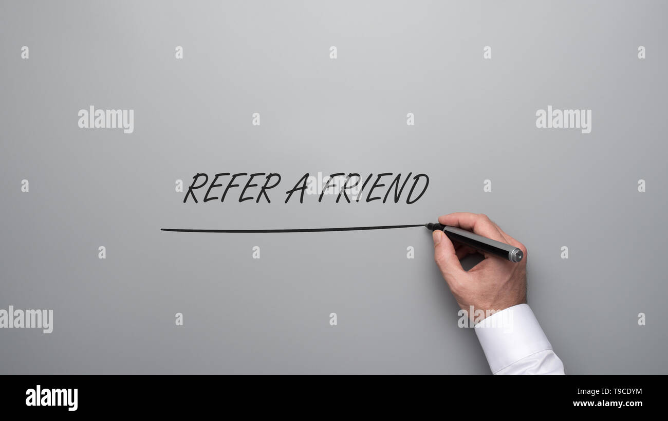 Male hand writing a Refer a friend sign on a grey background with black ...