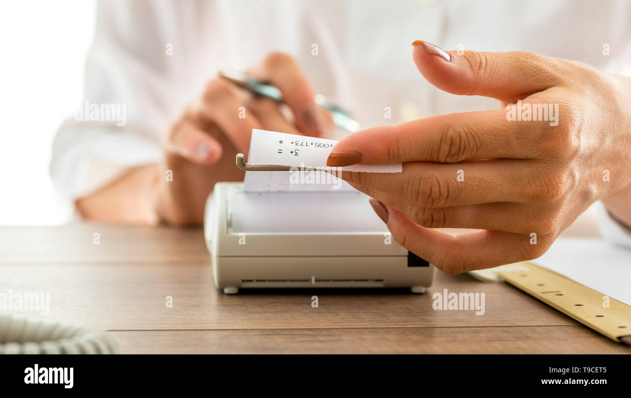 Closeup of a woman holding a printout receipt as it comes out of adding ...