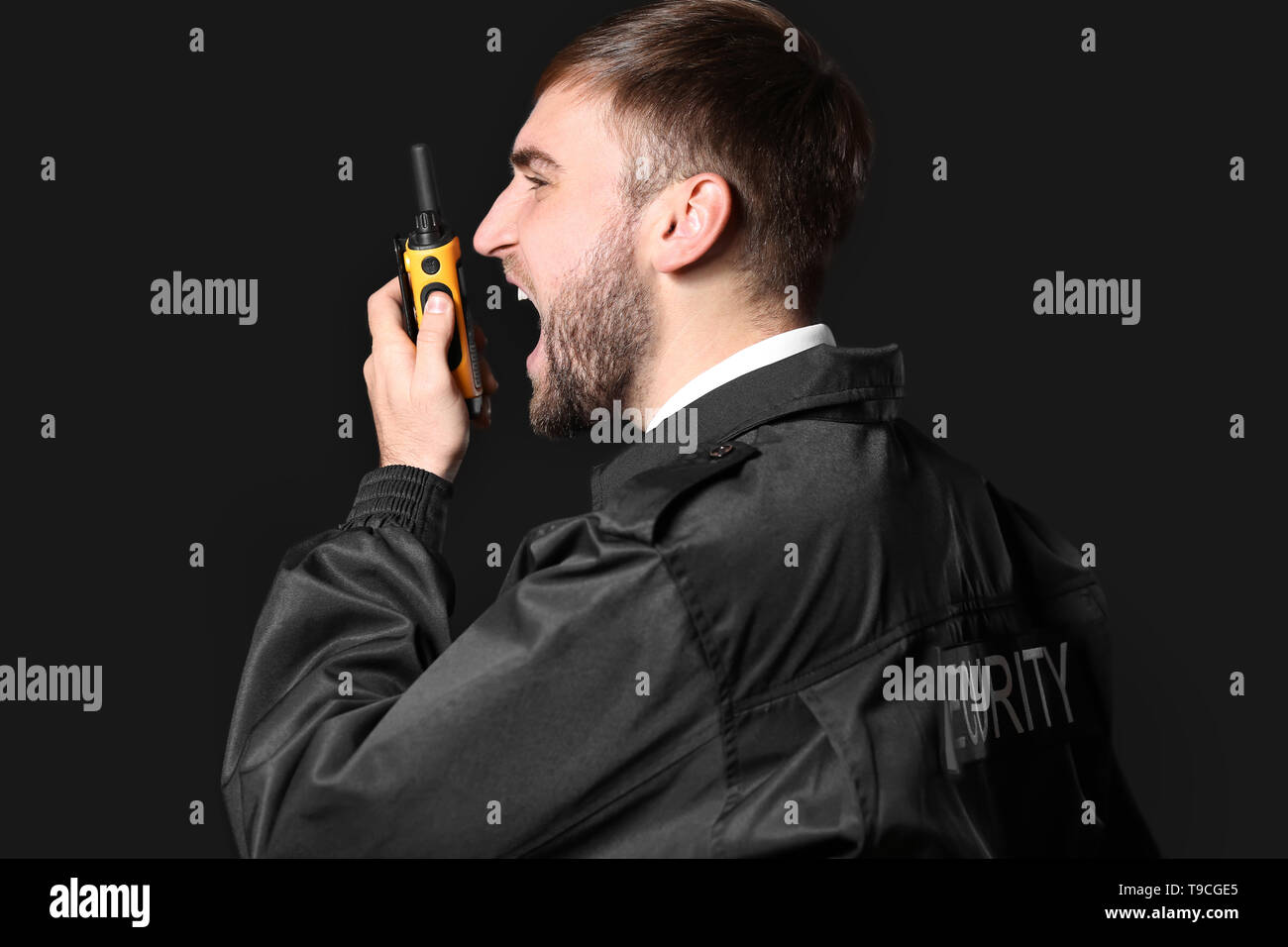 Male security guard with portable radio transmitter on dark background ...