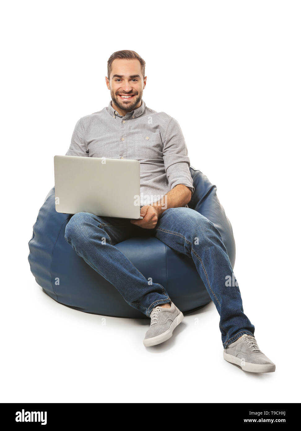 Young man with laptop sitting on beanbag chair against white background ...