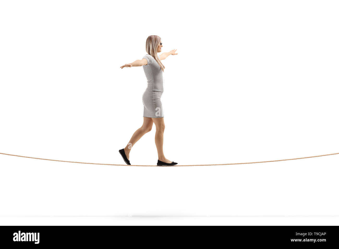 Full length profile shot of a young blond woman walking on a rope with ...