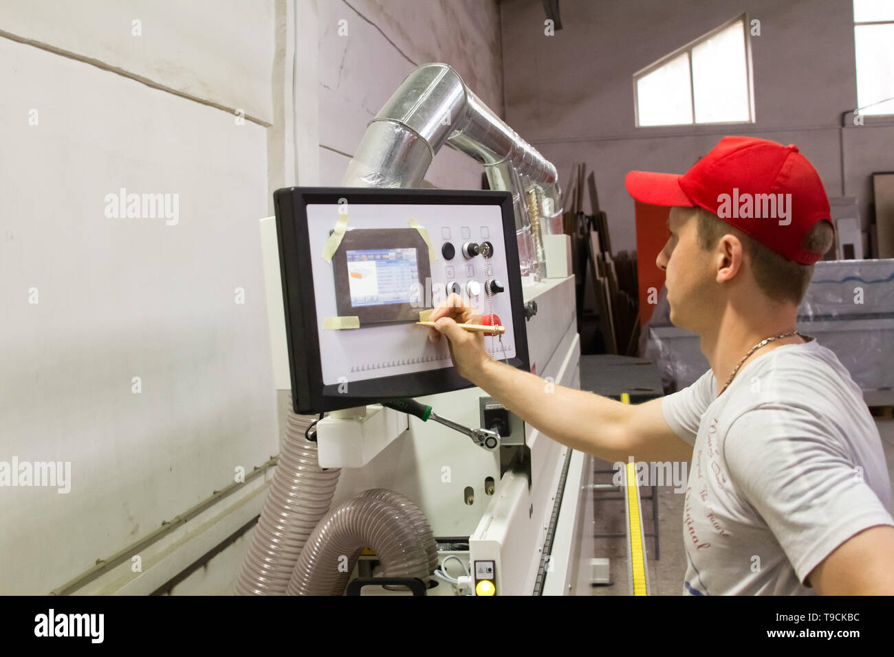 A male engineer controls the work of the machine in the furniture shop ...