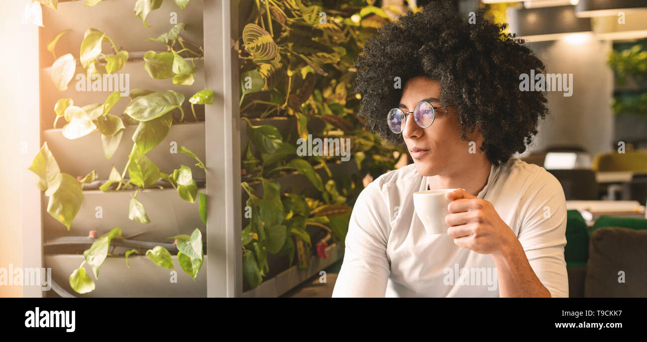 Dreamy black millennial guy drinking coffee in cafeteria Stock Photo ...