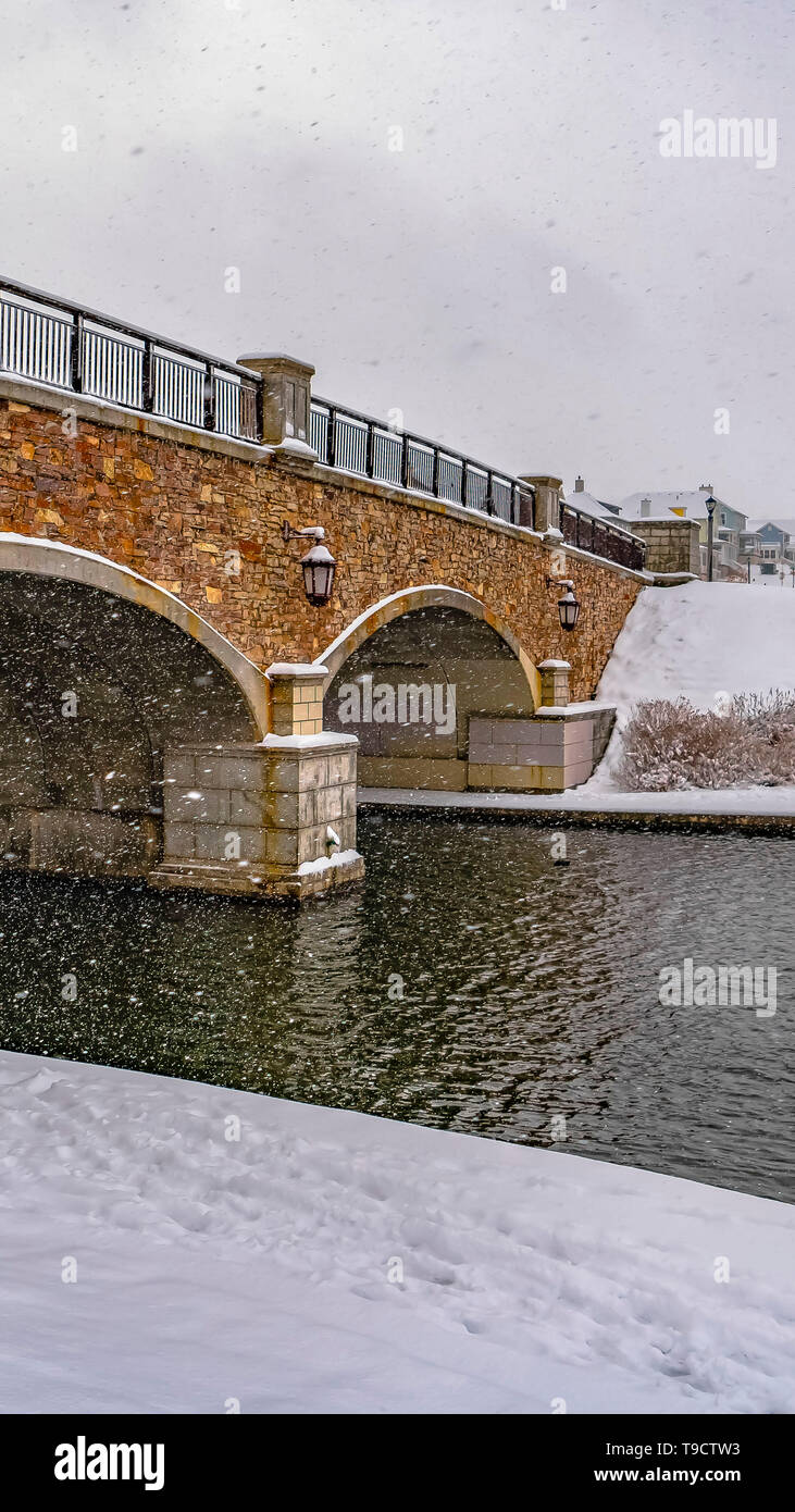 Vertical Stone arched bridge with lamps over a lake during winter in ...