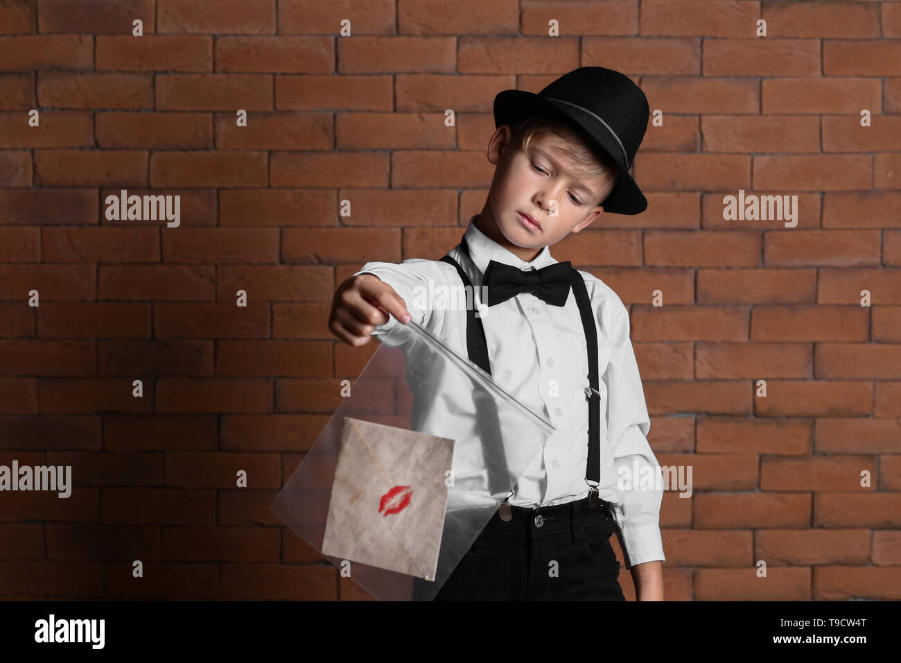 Cute little detective with evidence against brick wall Stock Photo - Alamy