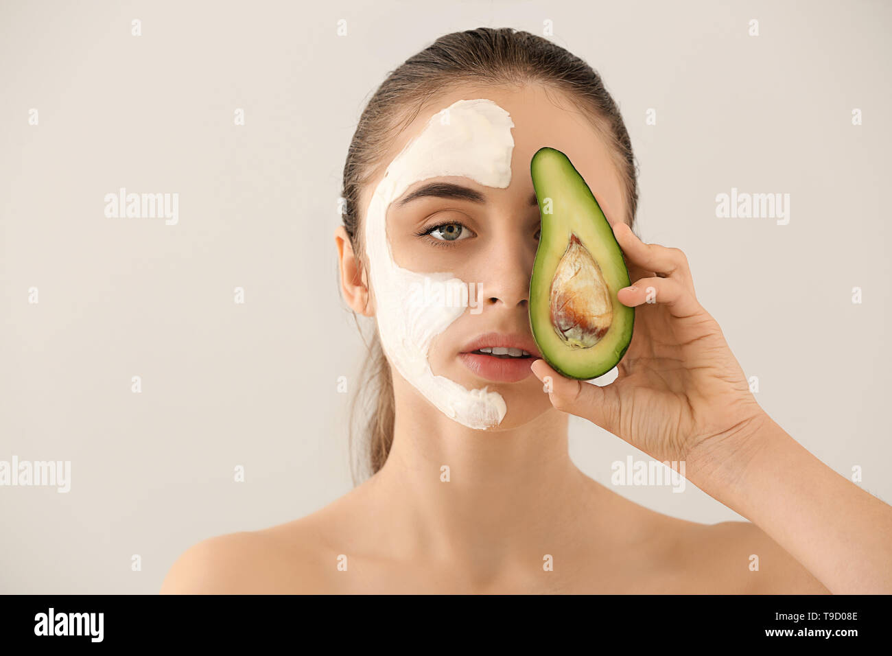 Beautiful young woman with avocado facial mask on light background ...