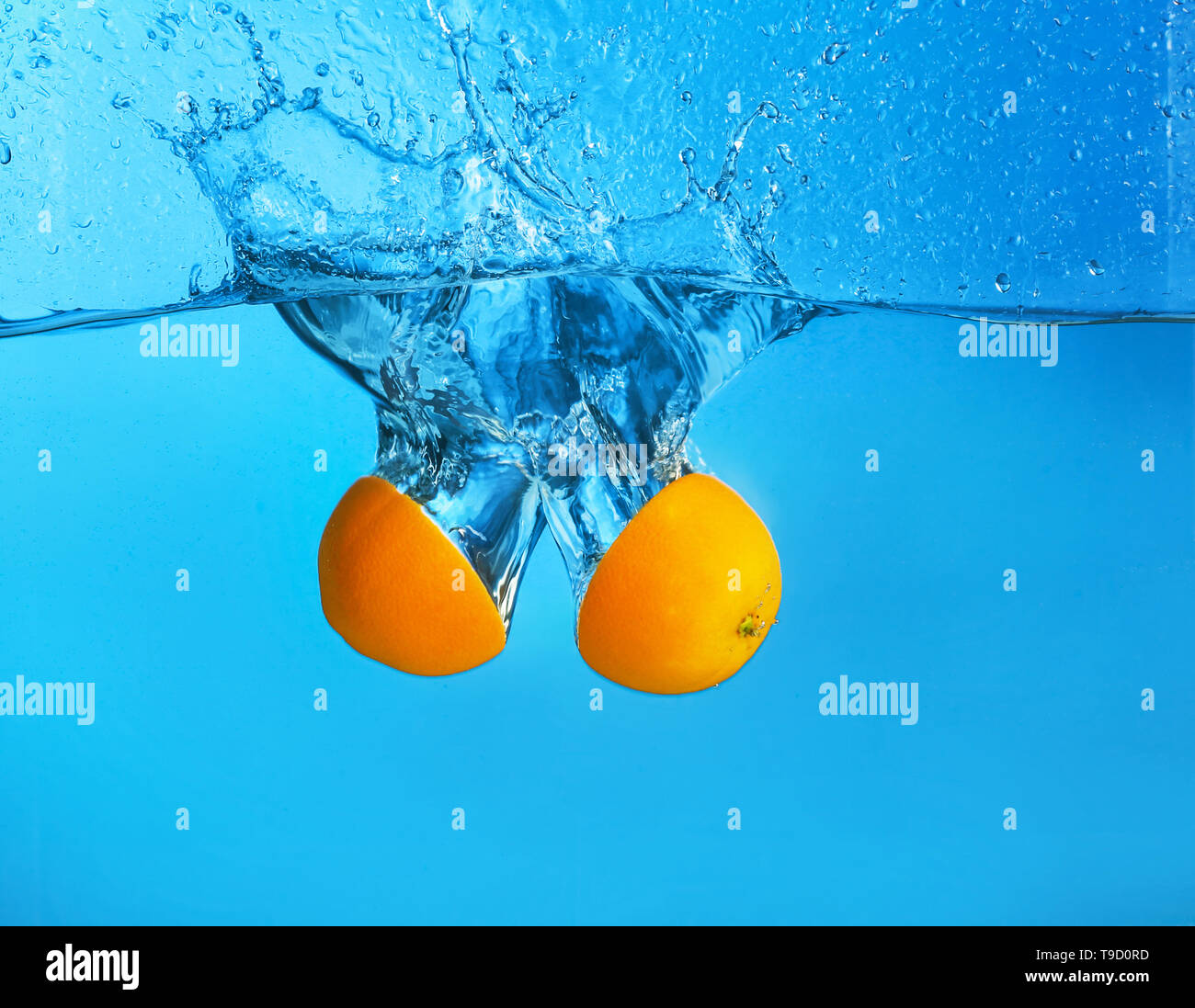 Falling of orange halves into water on color background Stock Photo - Alamy