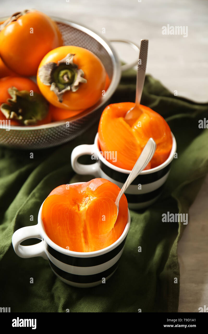 Cups and colander with tasty ripe persimmons on light table Stock Photo ...