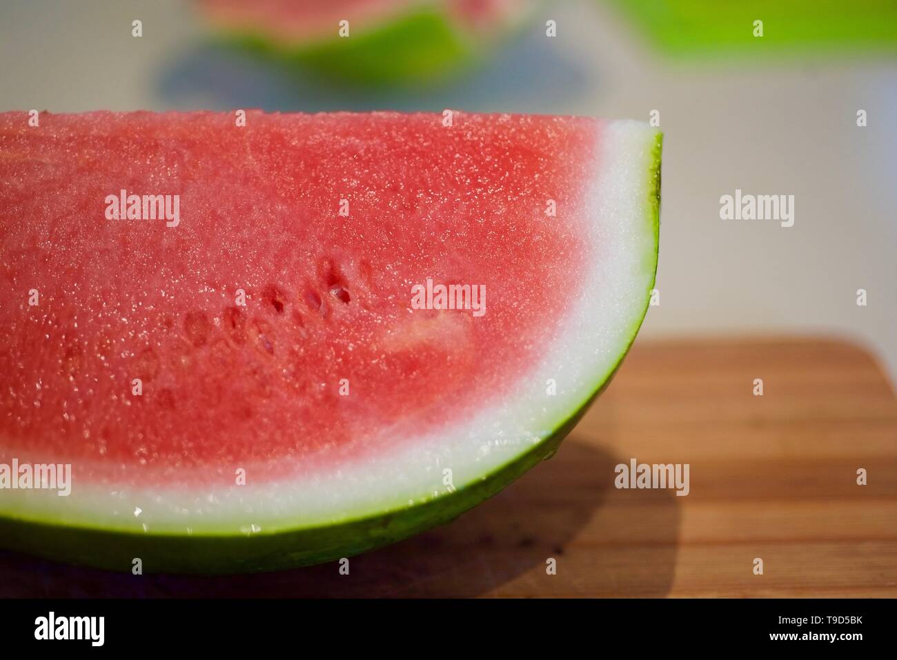 A juicy pink watermelon cut open into a quarter, on a wooden chopping ...