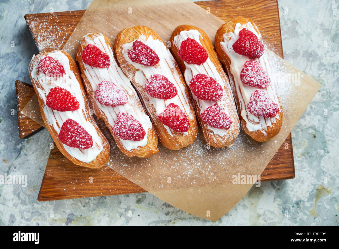 Cake eclair with cream and raspberry on a wooden board. Gray textured ...