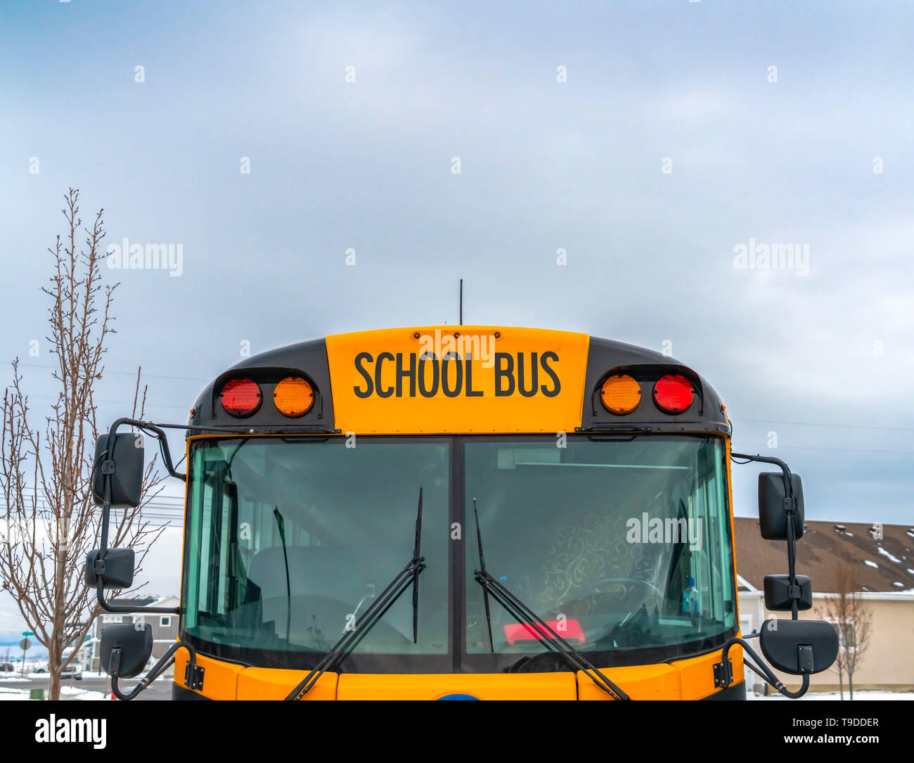 Front view of a yellow school bus with homes and cloudy sky in the ...