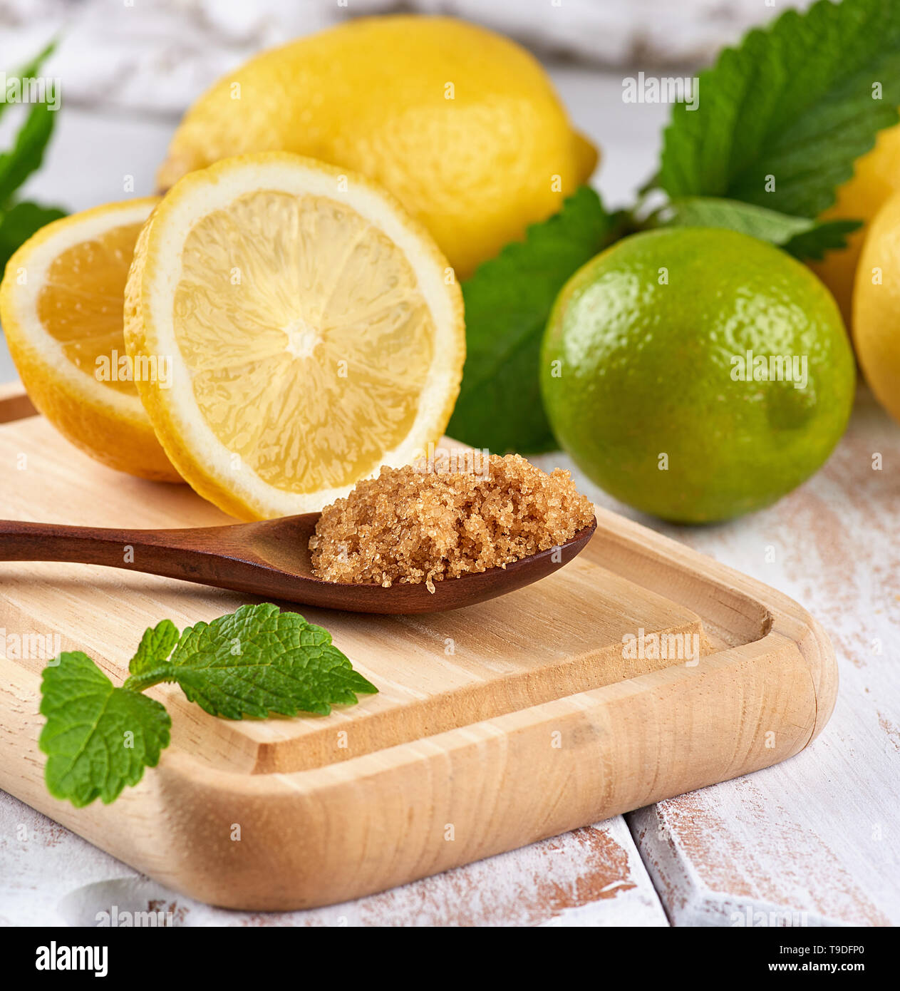 wooden spoon with brown sugar on the board, lemons and lime, mint for ...