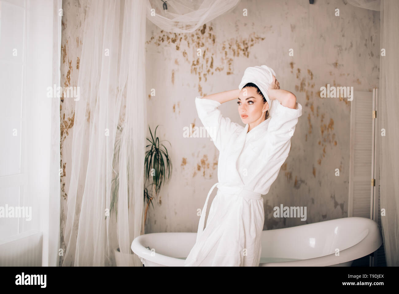 Serious Young Beautiful Woman Wearing White Bathrobe Standing In Modern