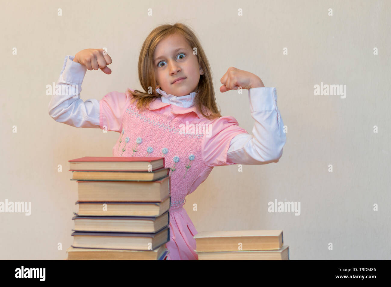 Concept The power of knowledge. A girl with a pile of books shows her ...