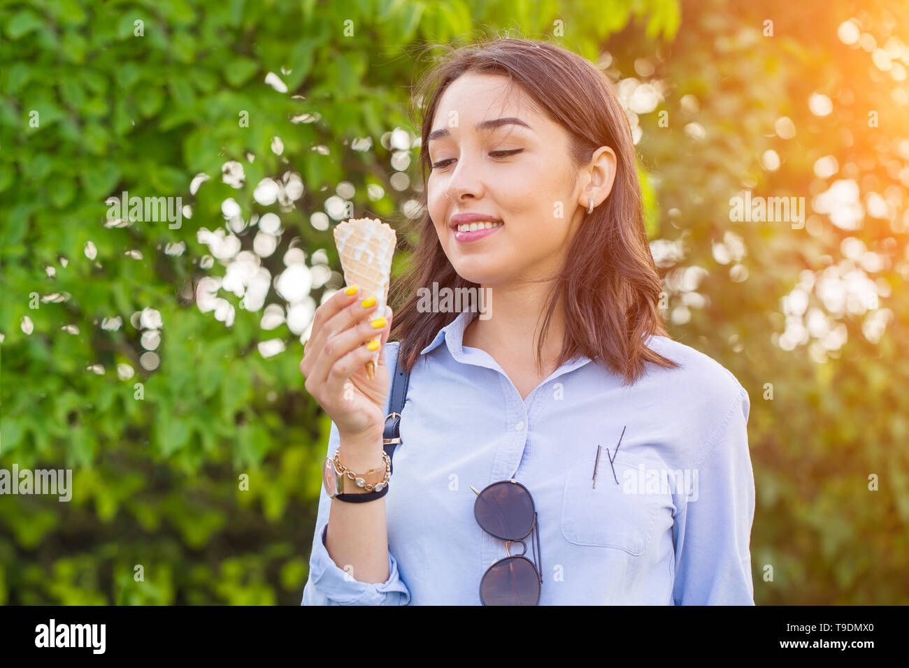 Cheerful brunette woman eating ice cream on nature background and ...