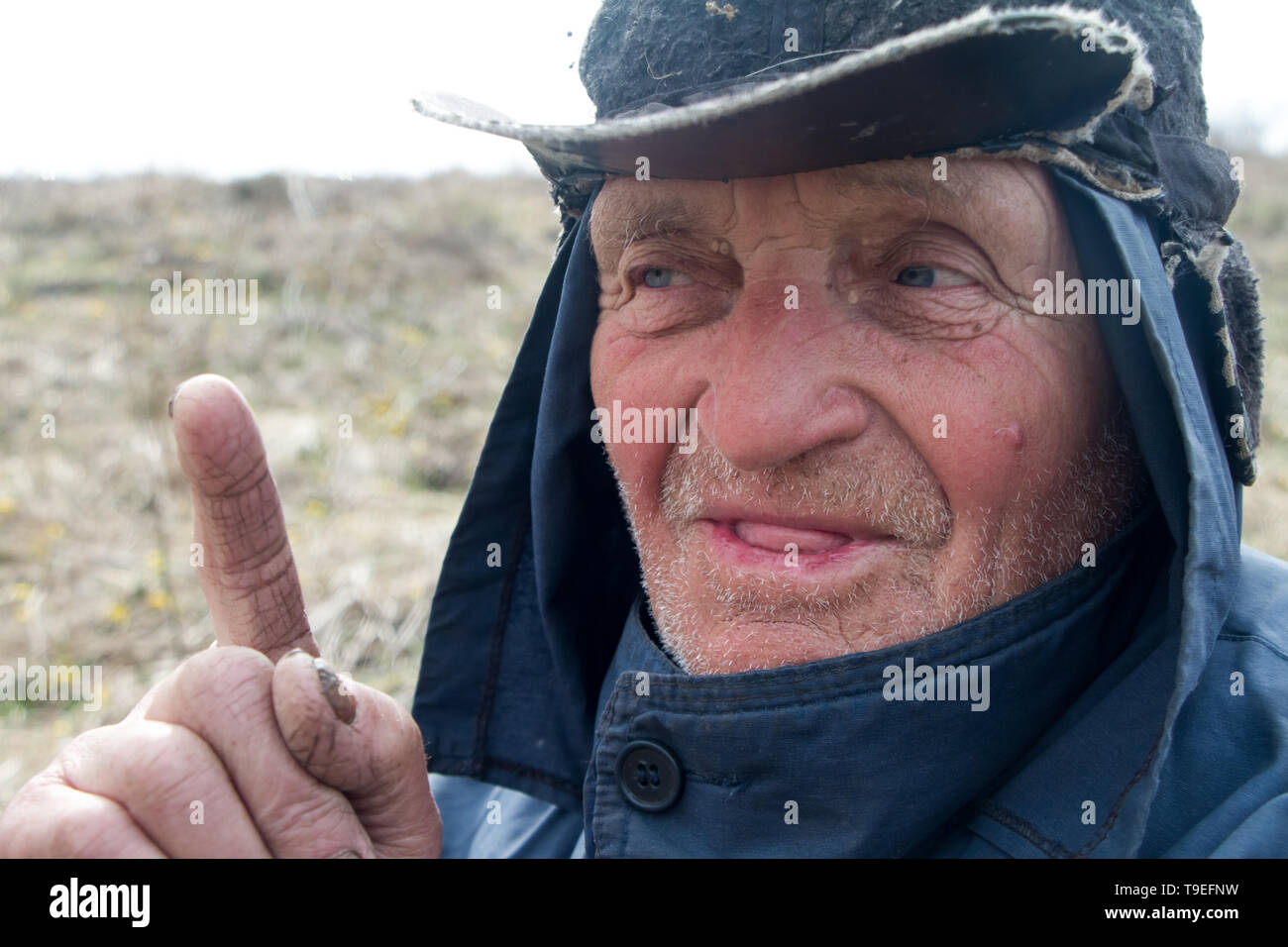 Portrait of an old man in a messy clothes and hat who raised his index ...