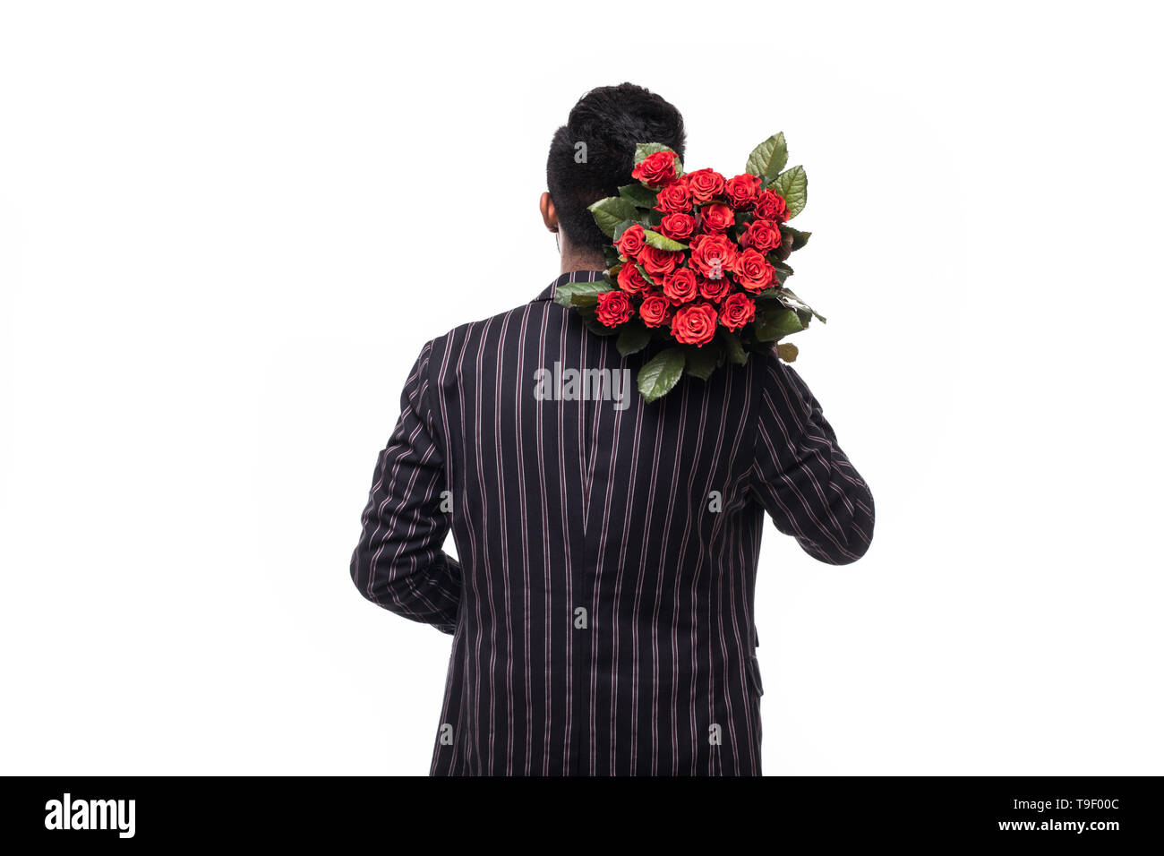 Handsome yound man in suit is standing with red roses behind the back ...