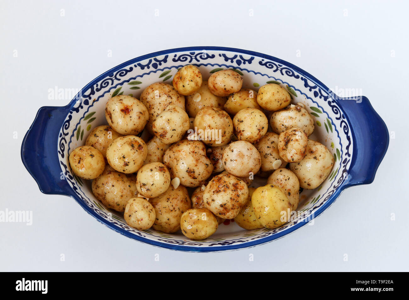 Young peeled potatoes in spices prepared for roasting in a ceramic form ...