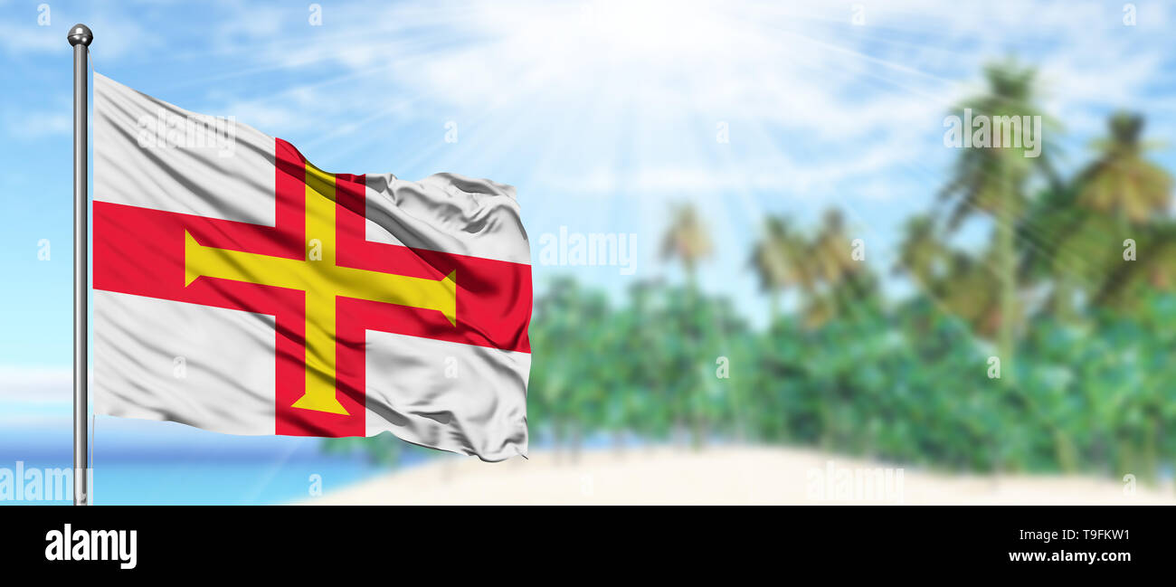 Waving Guernsey flag in the sunny blue sky with summer beach background ...