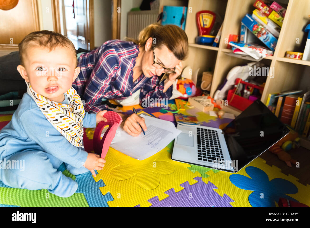 Mother working on her computer while taking care of her baby at home ...
