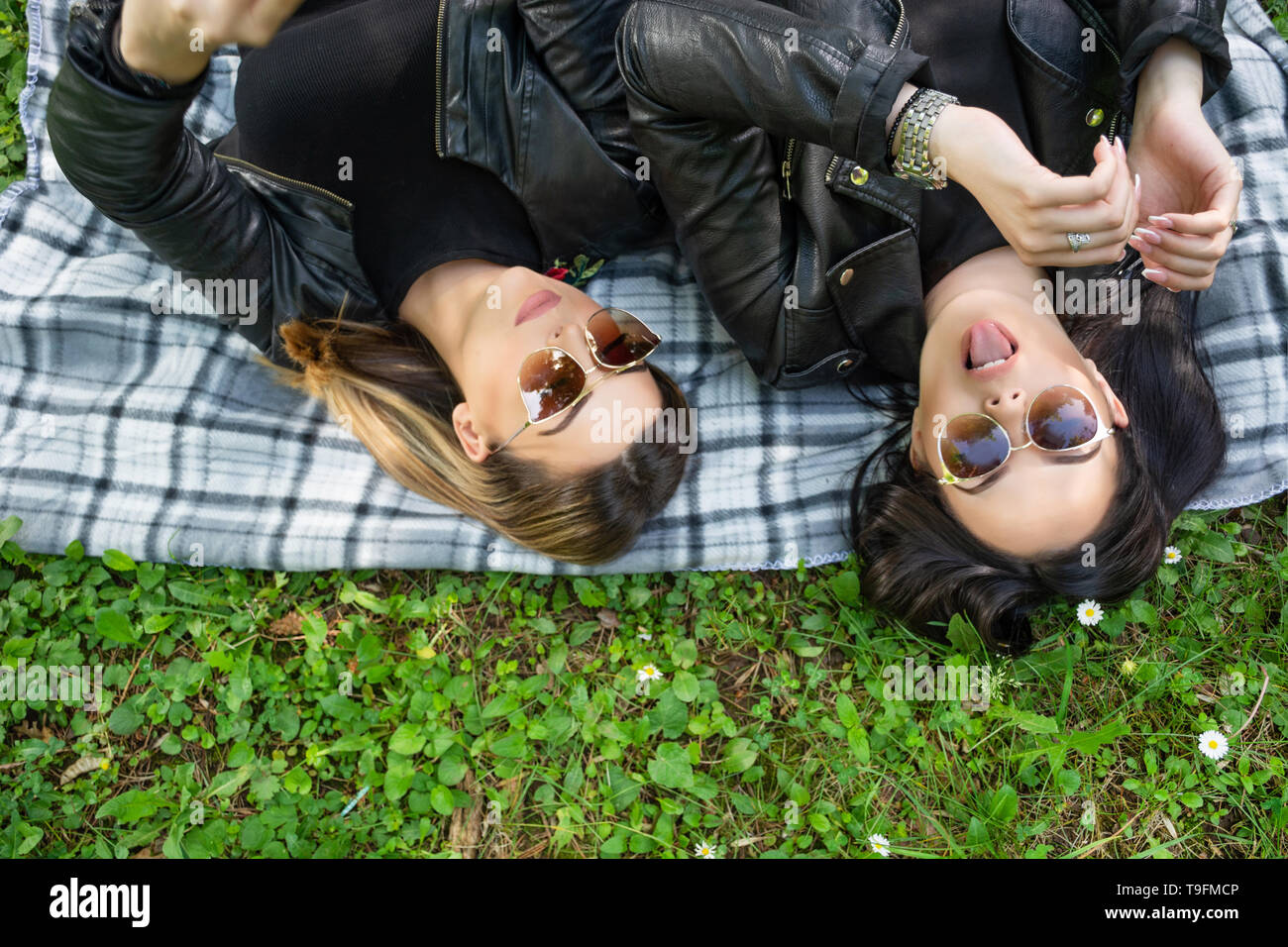 Two happy girls lying down on blanket in a green meadow on a spring day ...