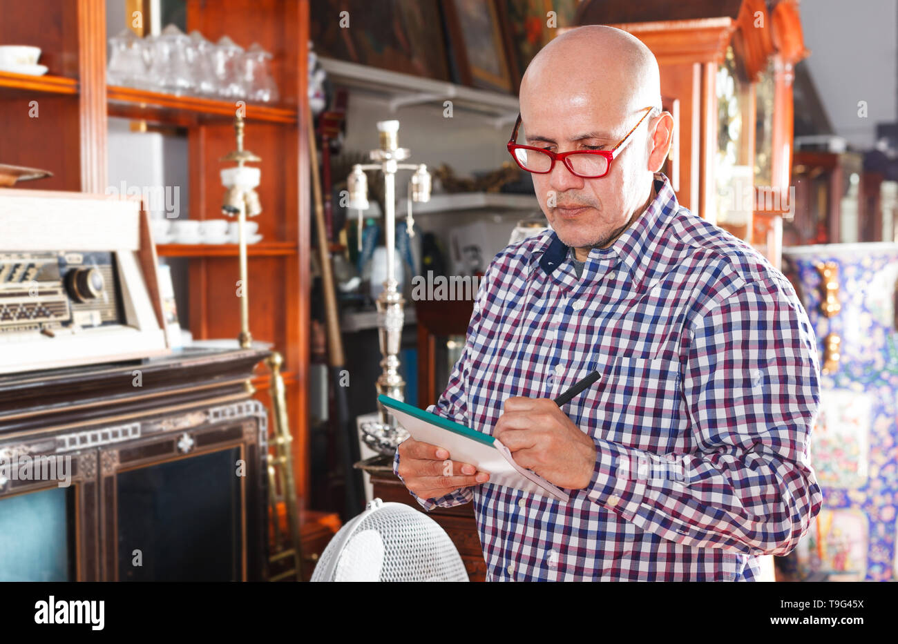 Focused mature male collector of rare items making notes in notepad ...
