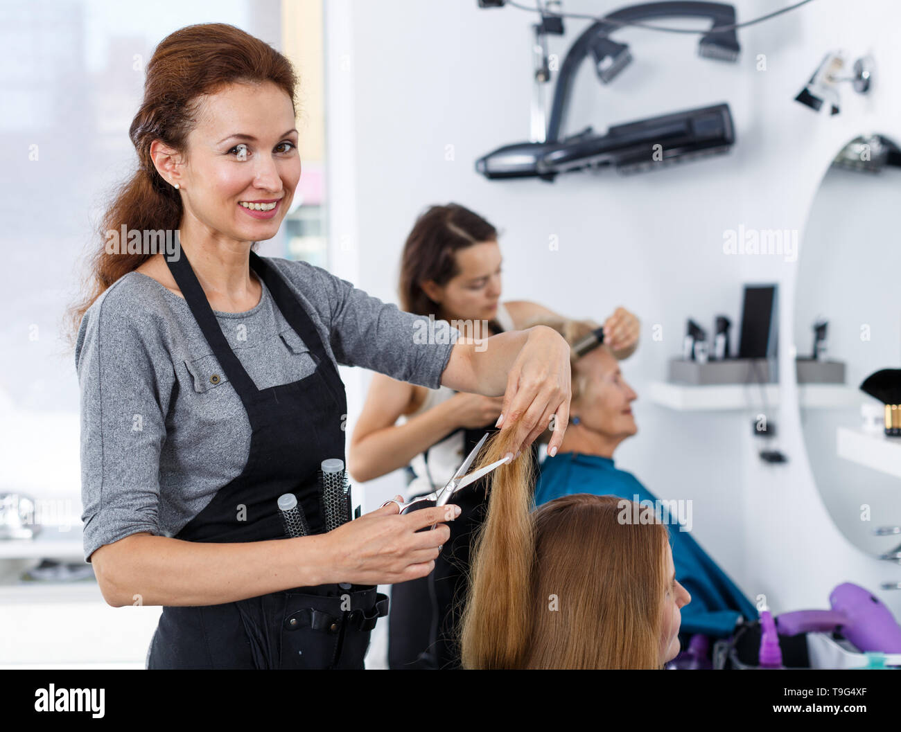 Skillful hairdresser woman doing styling of long-haired teen girl at ...