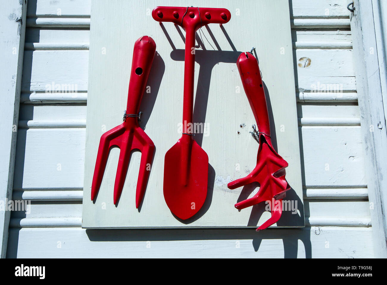 The small red coloured garden tools are hanging on the white wall Stock ...