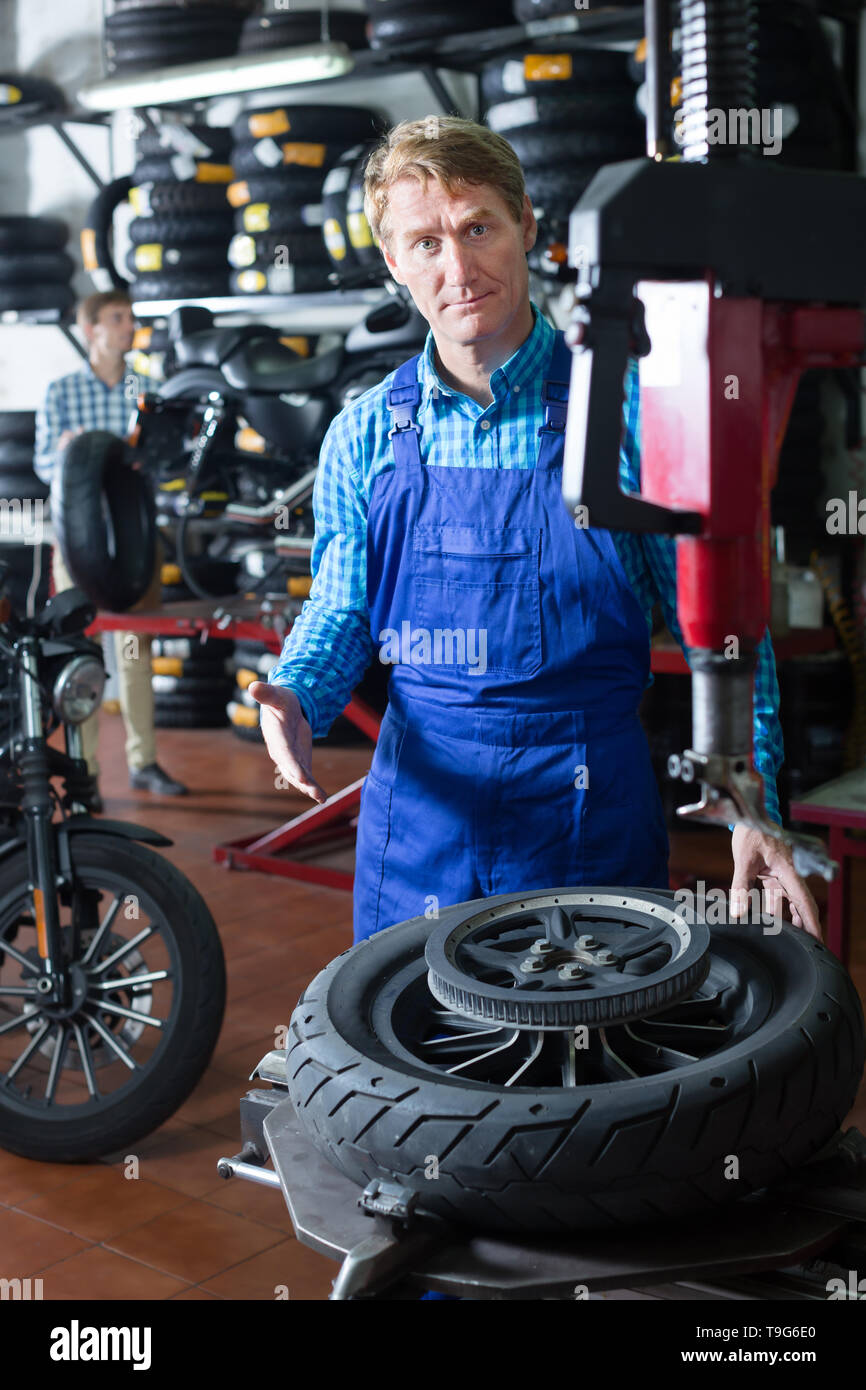 Attentive adult mechanic man standing with motorcycle wheel in shop ...