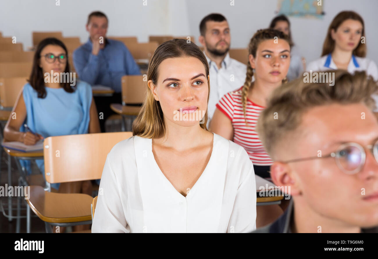 Portrait of young woman attentively listening to lecture in classroom ...