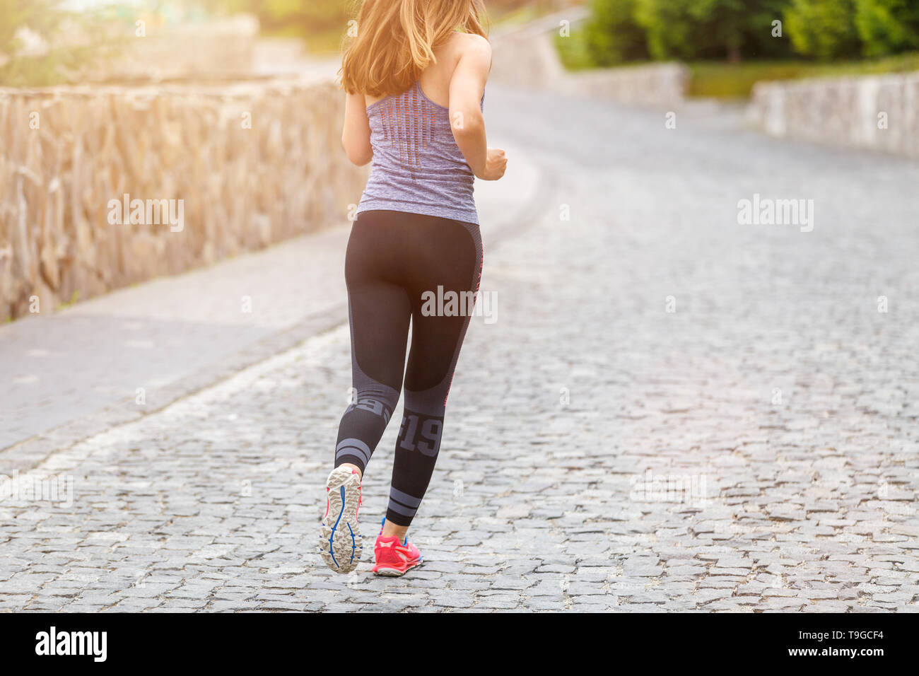 Back view of running woman on cobbled road with copy space aside. Rear ...