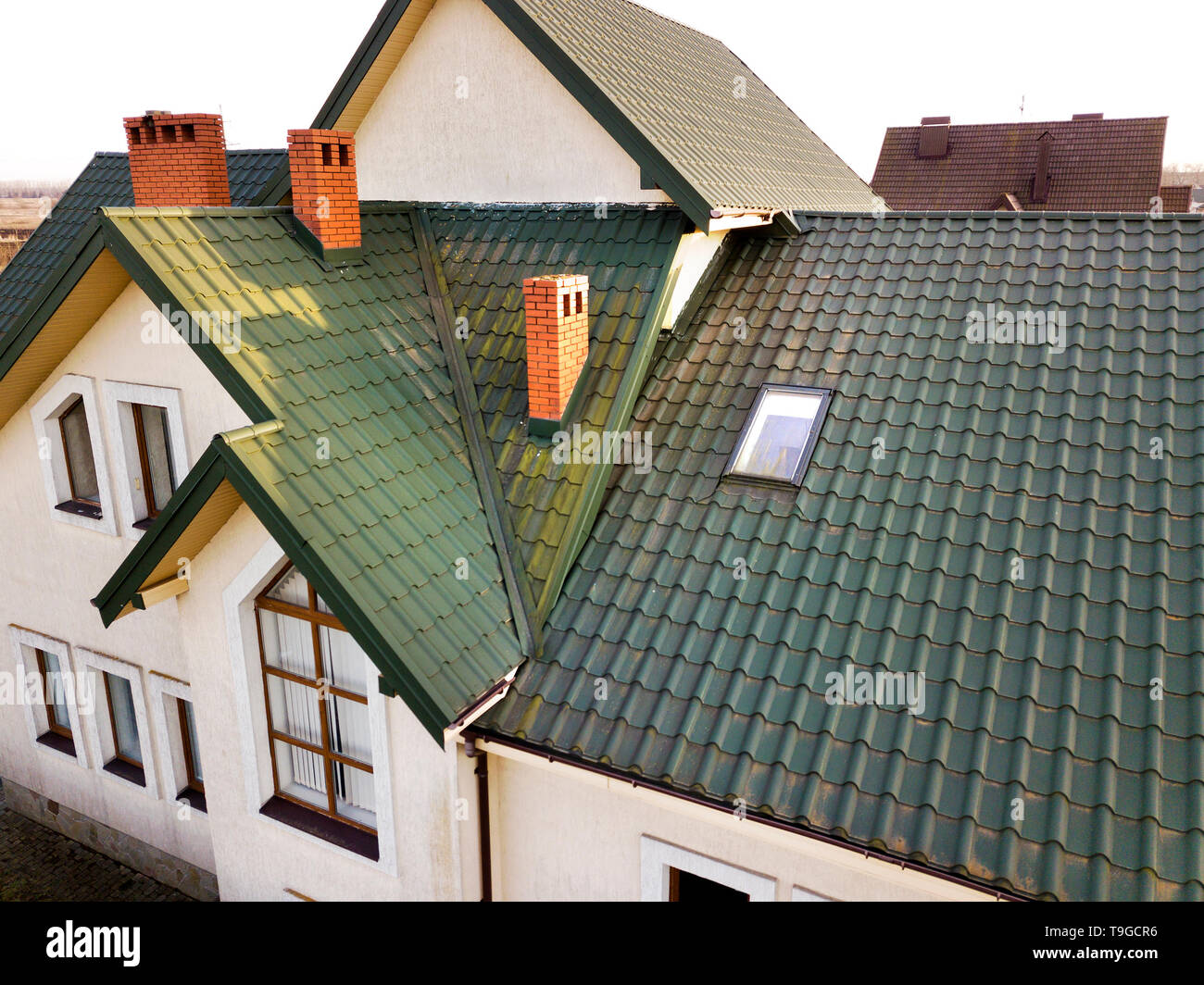 Green metal shingled house roof with attic plastic window and brick ...