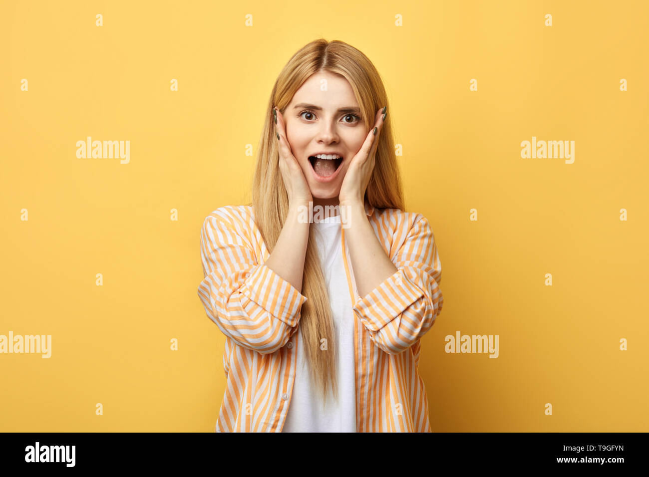 attractive emotional delighted blonde woman with palms on cheeks ...