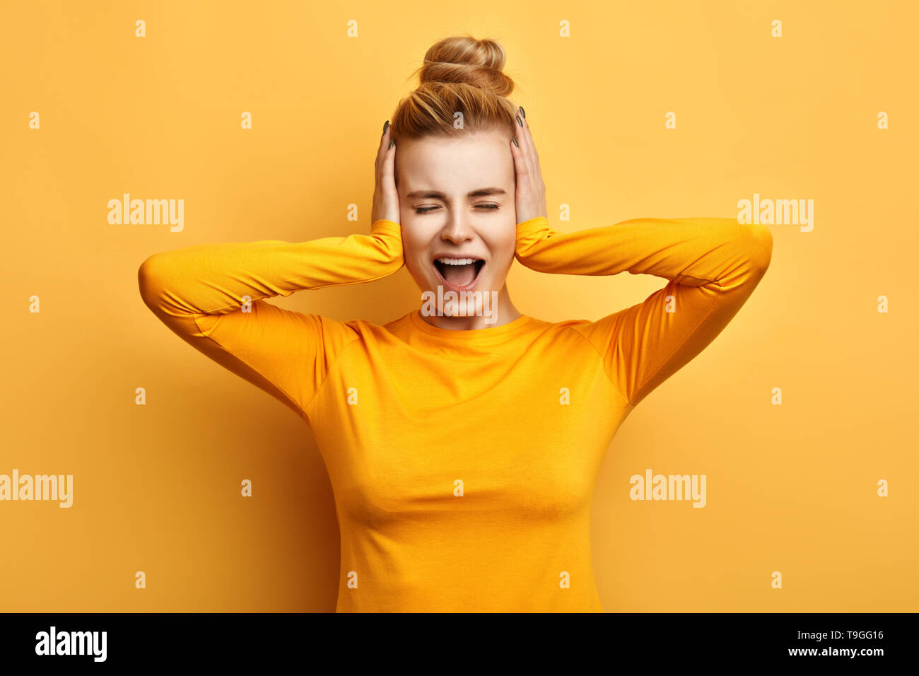 Young woman in stylish yellow sweater screaming in terror with hands on ...