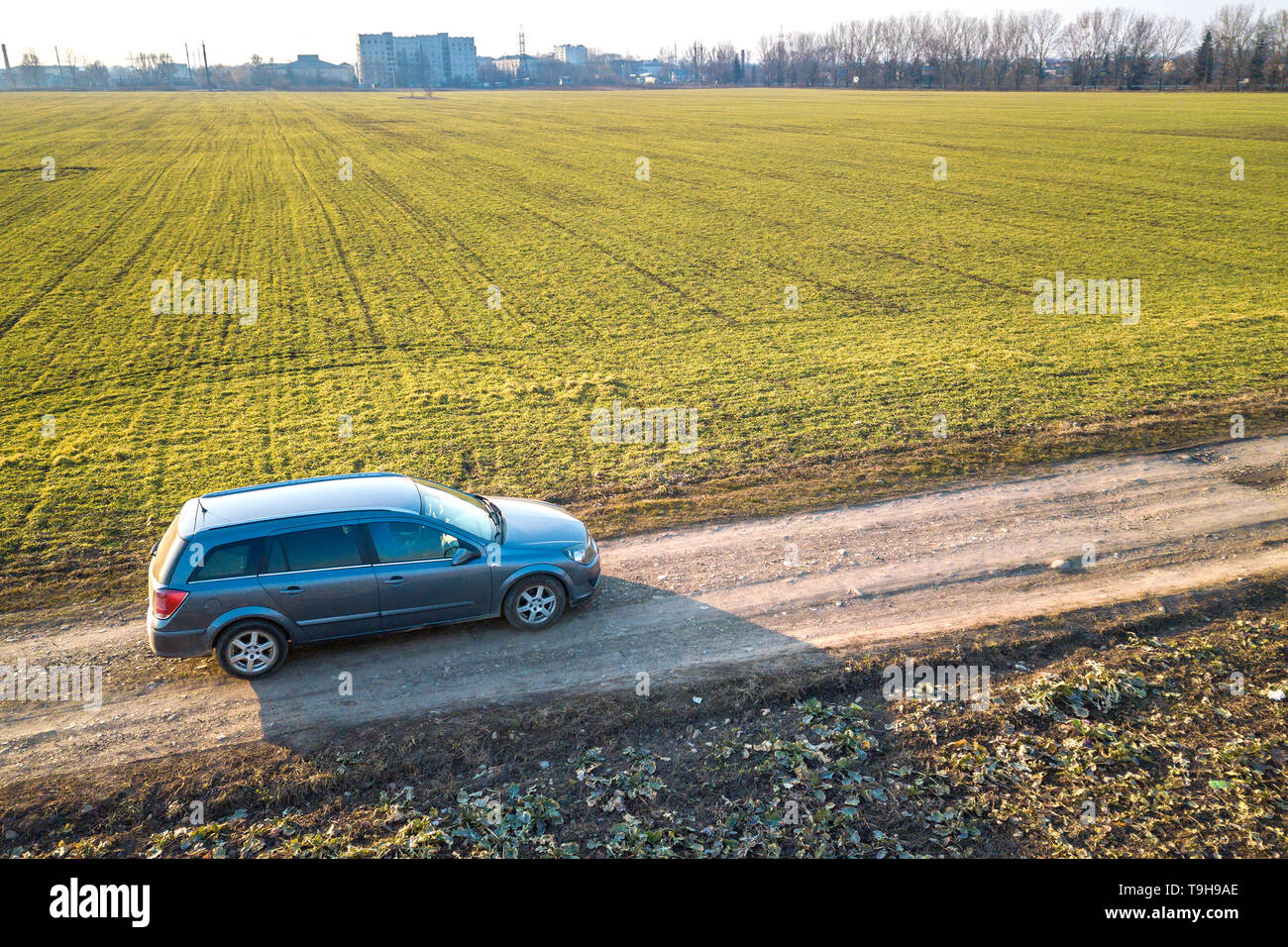 Aerial view of car driving by straight ground road through green fields ...