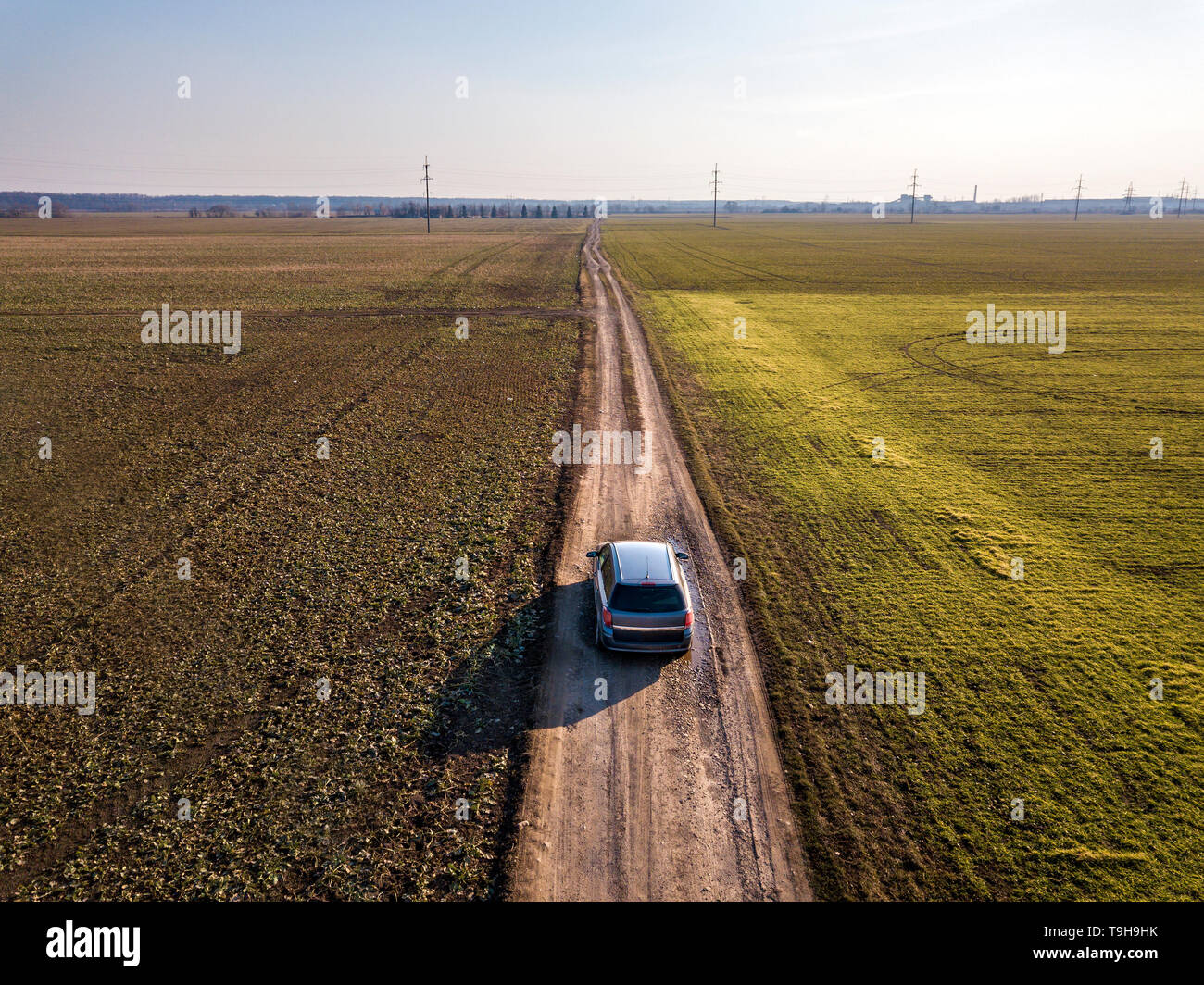 Aerial view of car driving by straight ground road through green fields ...