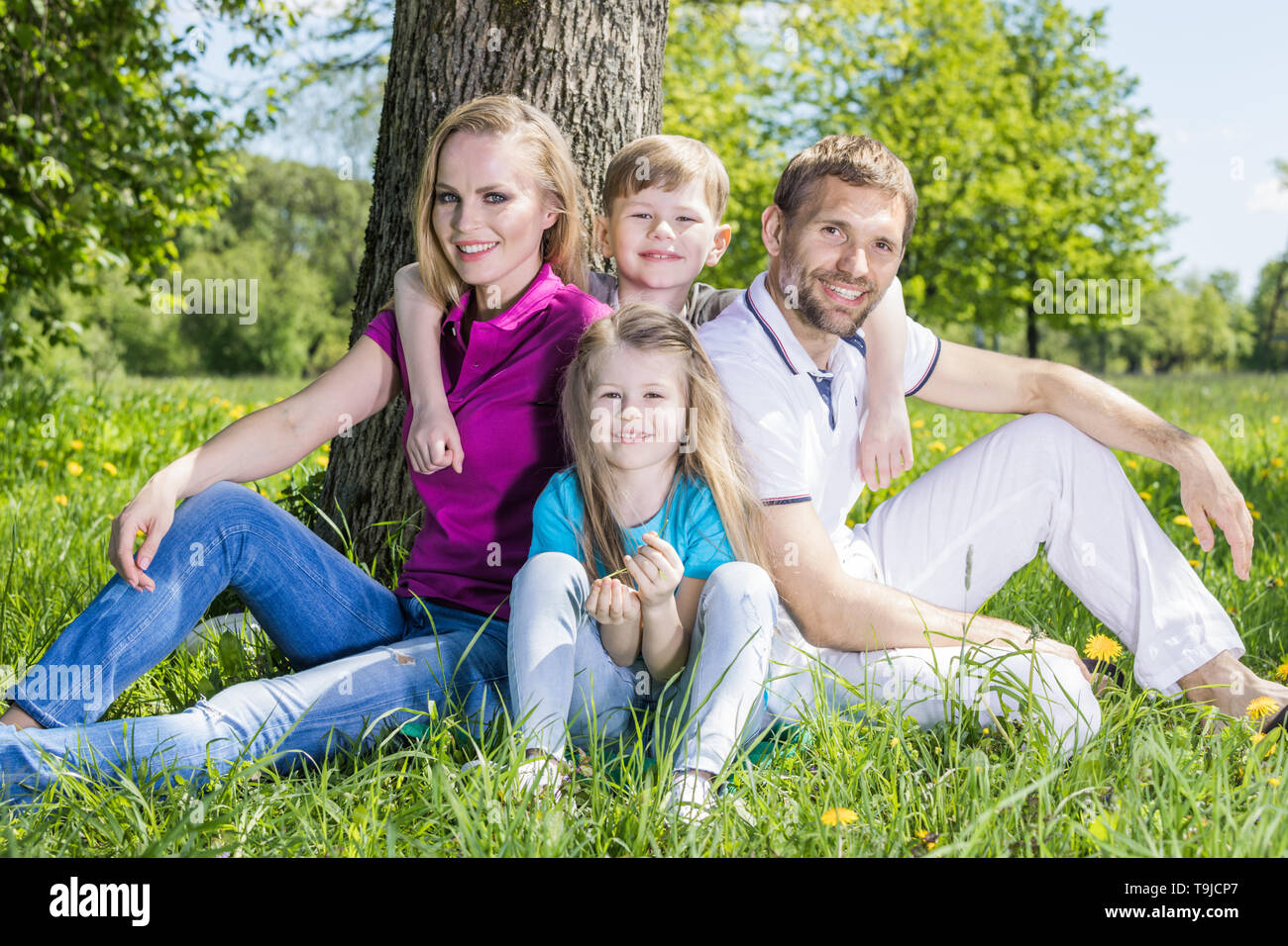 Parents and two children sitting under the tree on summer lawn. Happy ...