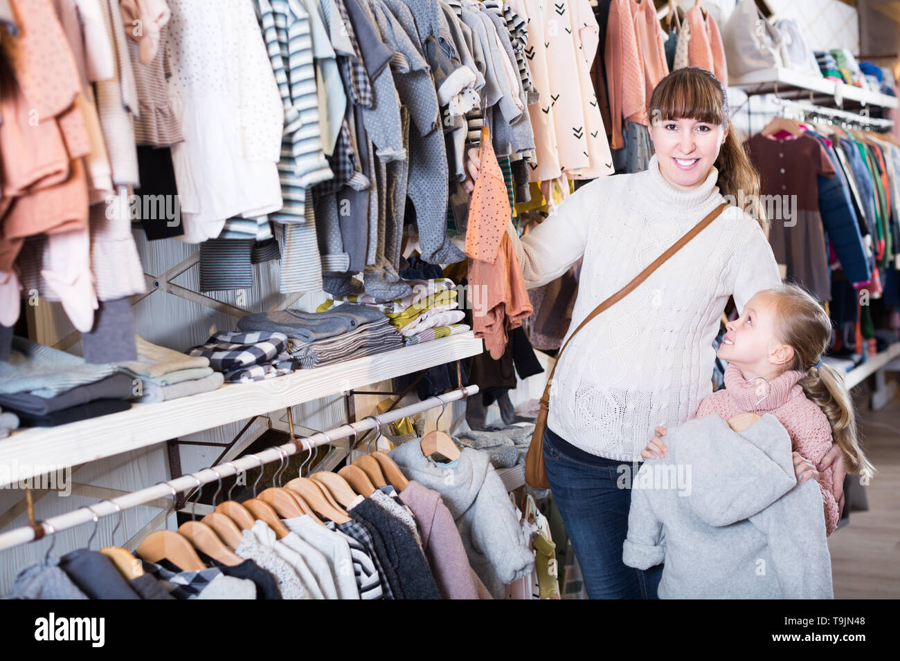 Smiling female and girl child choosing children’s clothes in store ...